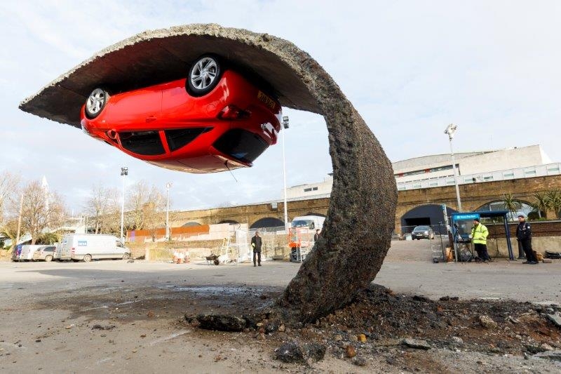 A parked car hangs 15 feet in the air while still attached to the road ...